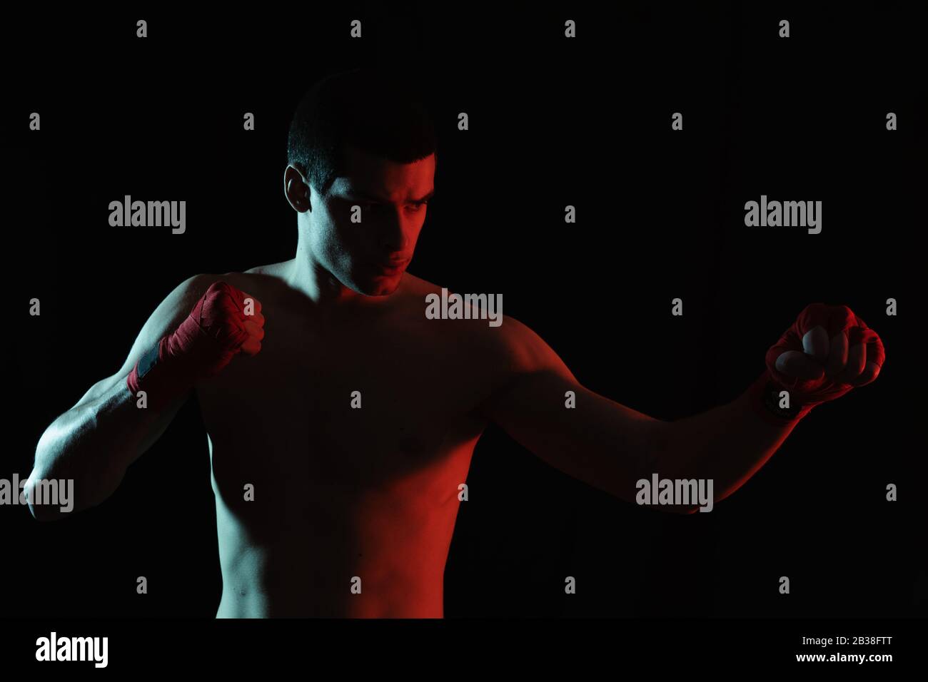 Athletic boxer punching with determination in a dark space with red and ...