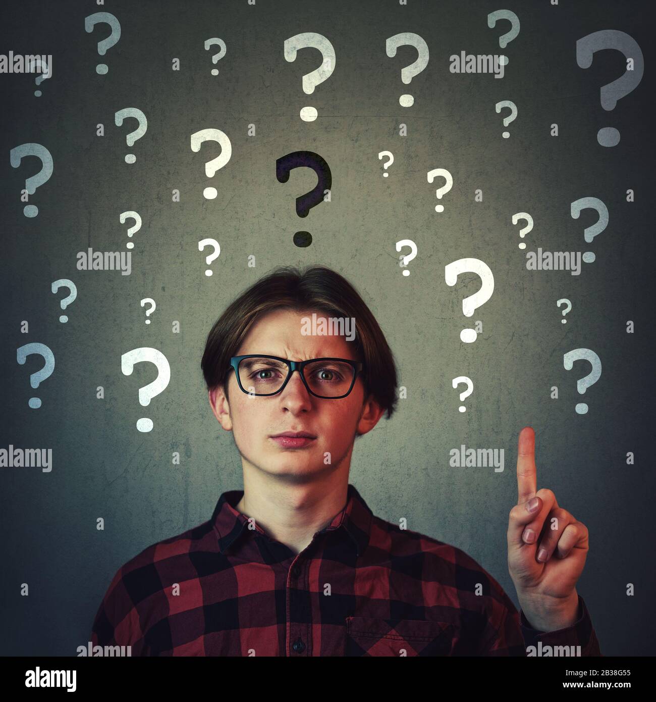 Confused adolescent guy, wearing eyeglasses gesturing index finger up ...