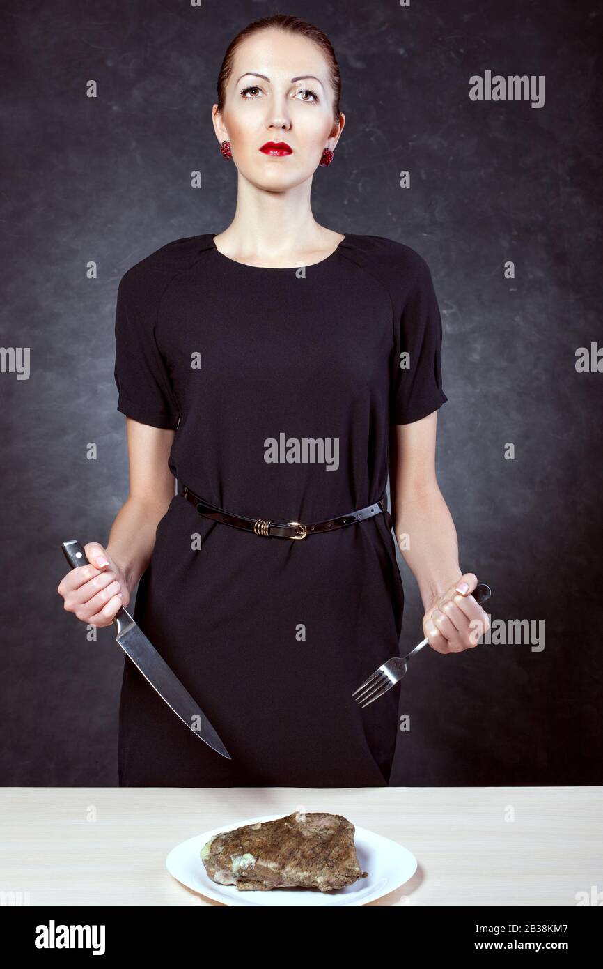 Young beautiful woman holding a knife and a fork in her hands. In front ...