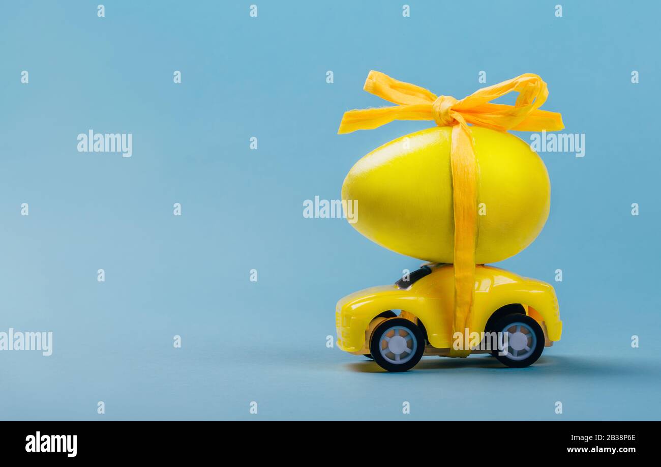 Yellow car toy with colored egg on top tied by string with bow on blue ...