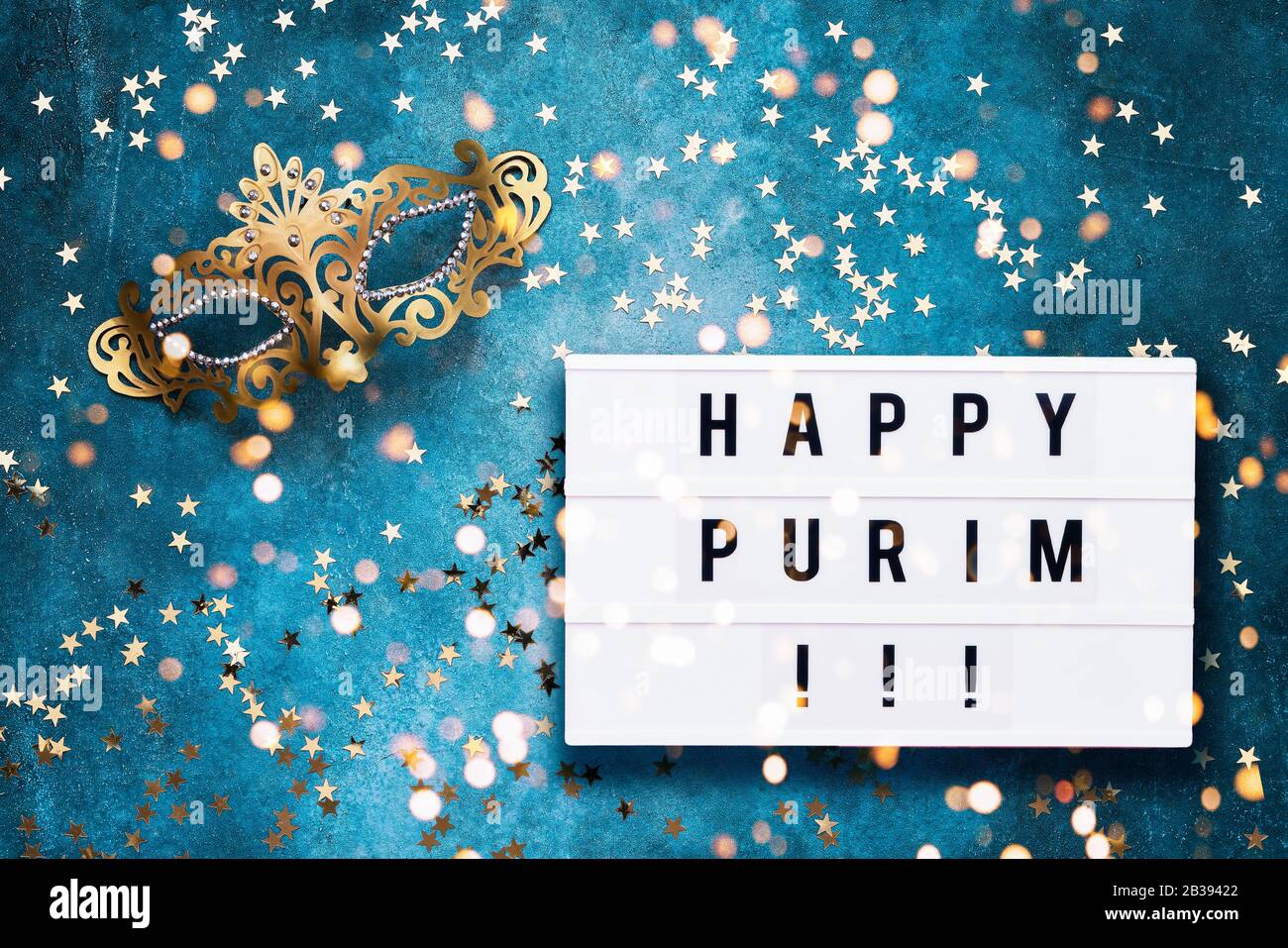 Happy Purim written in light box, golden carnival mask and golden stars ...