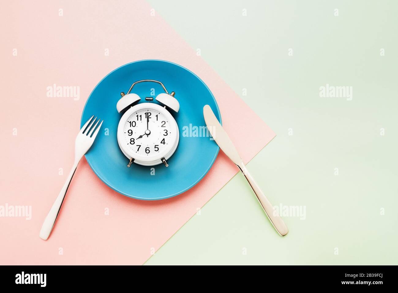 Intermittent fasting concept. White alarm clock on empty blue dish with ...