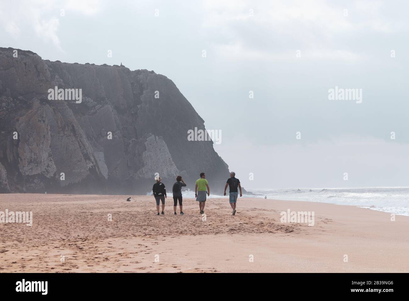 Beach with a big cliff in background in a winter day with four people ...