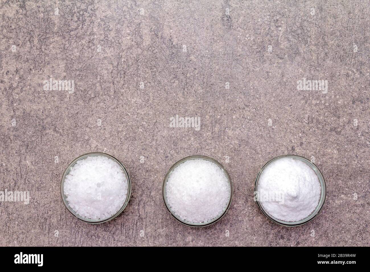 Three types of sea salt - large, medium and small. Top view, on a gray ...