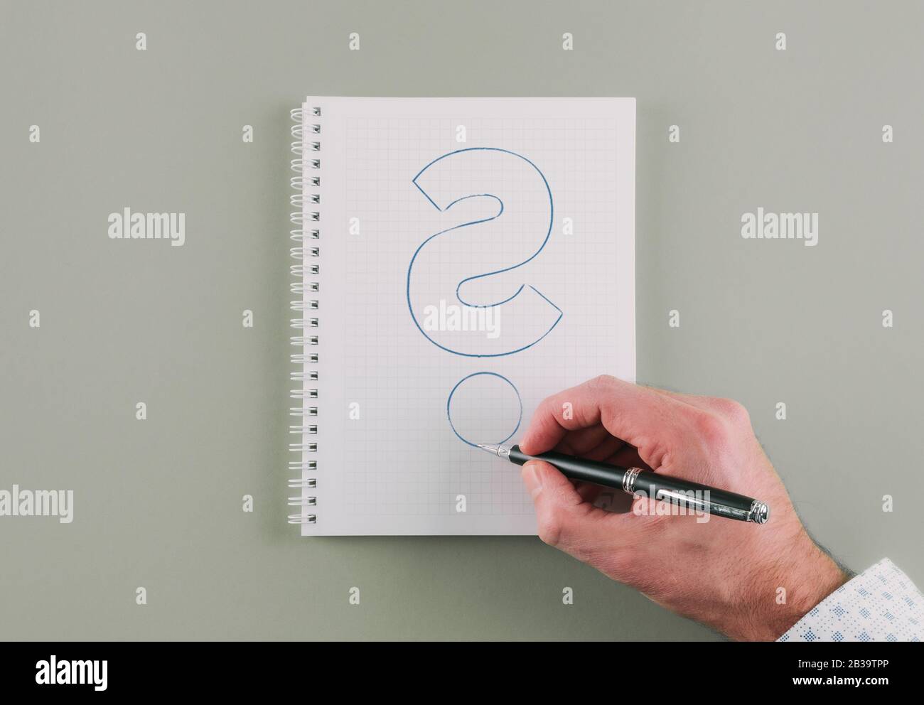 top view of hand holding ballpoint pen drawing question mark on spiral ...