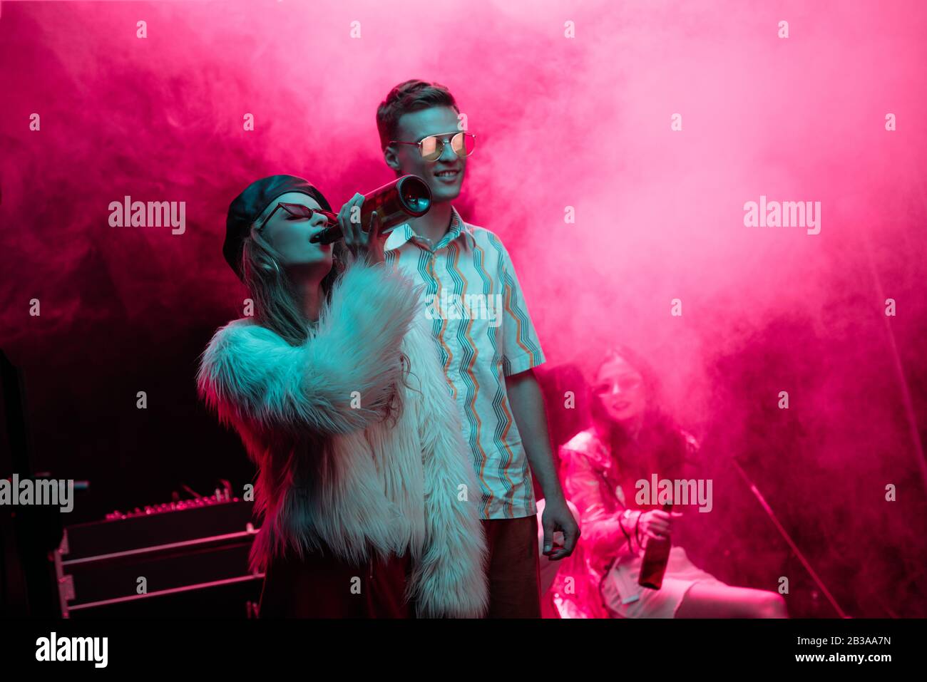 beautiful young woman drinking beer near man in nightclub during rave ...