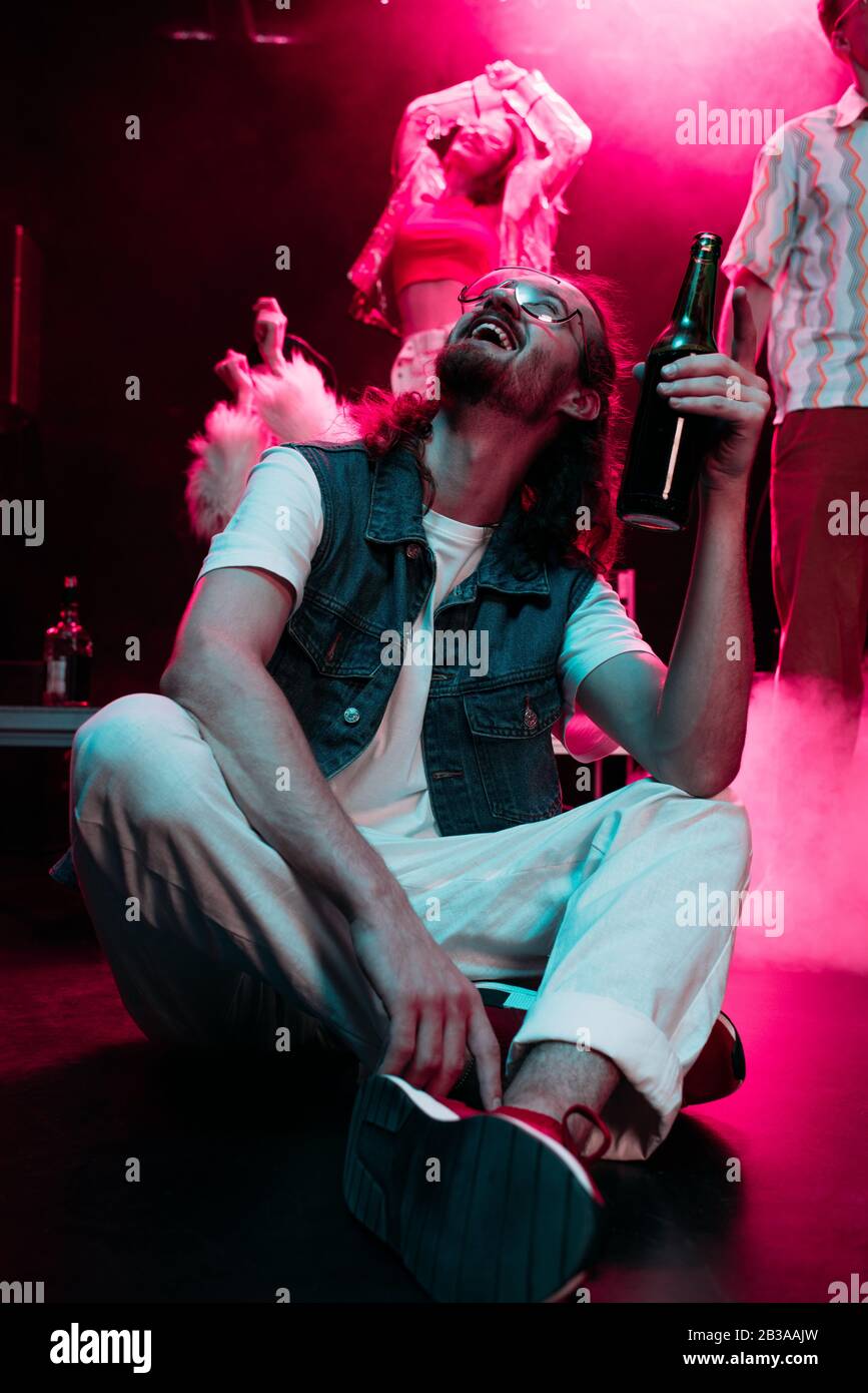 happy man in sunglasses with bottle of alcohol during rave in nightclub ...