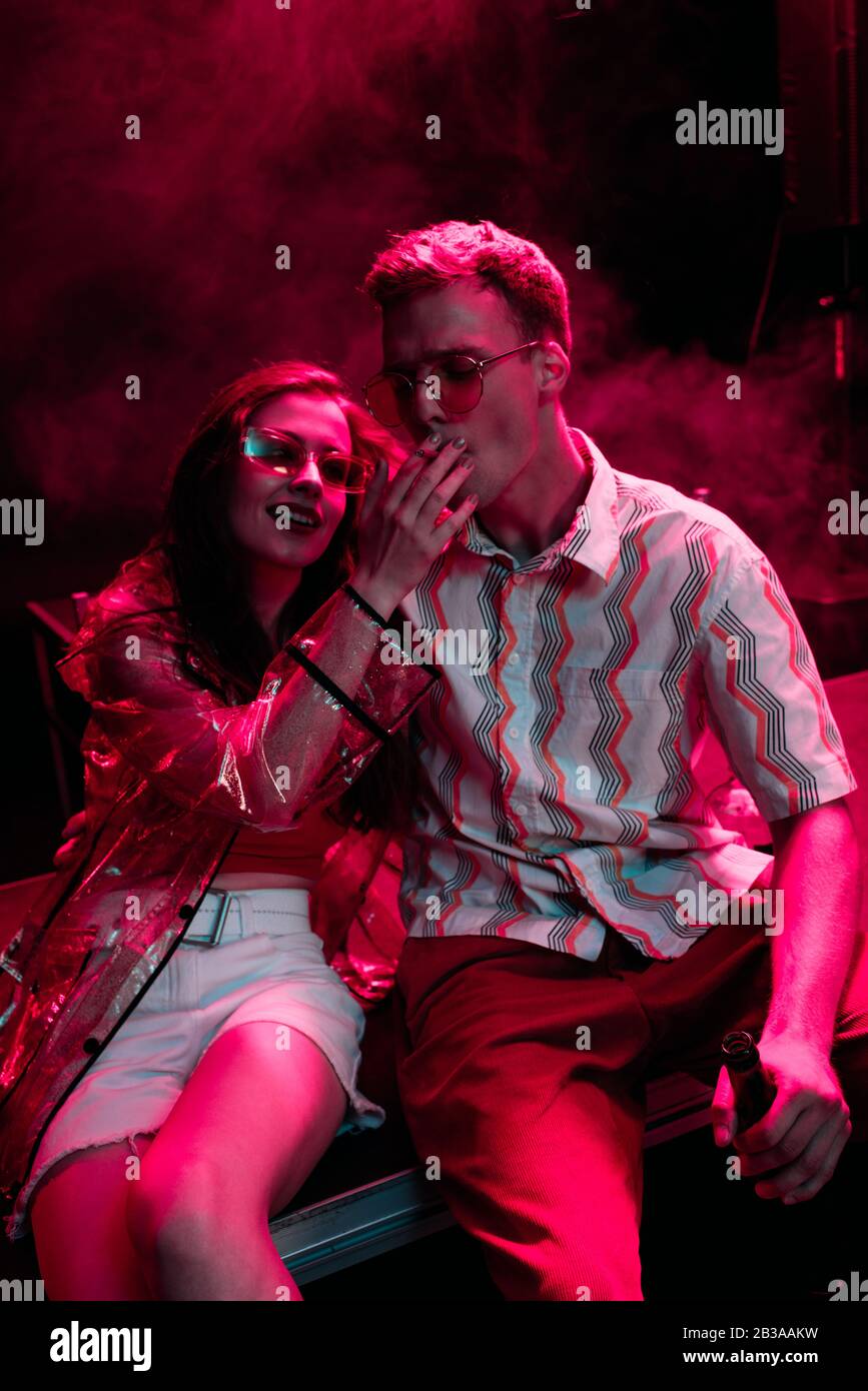 man smoking cigarette near young woman during rave party in nightclub ...