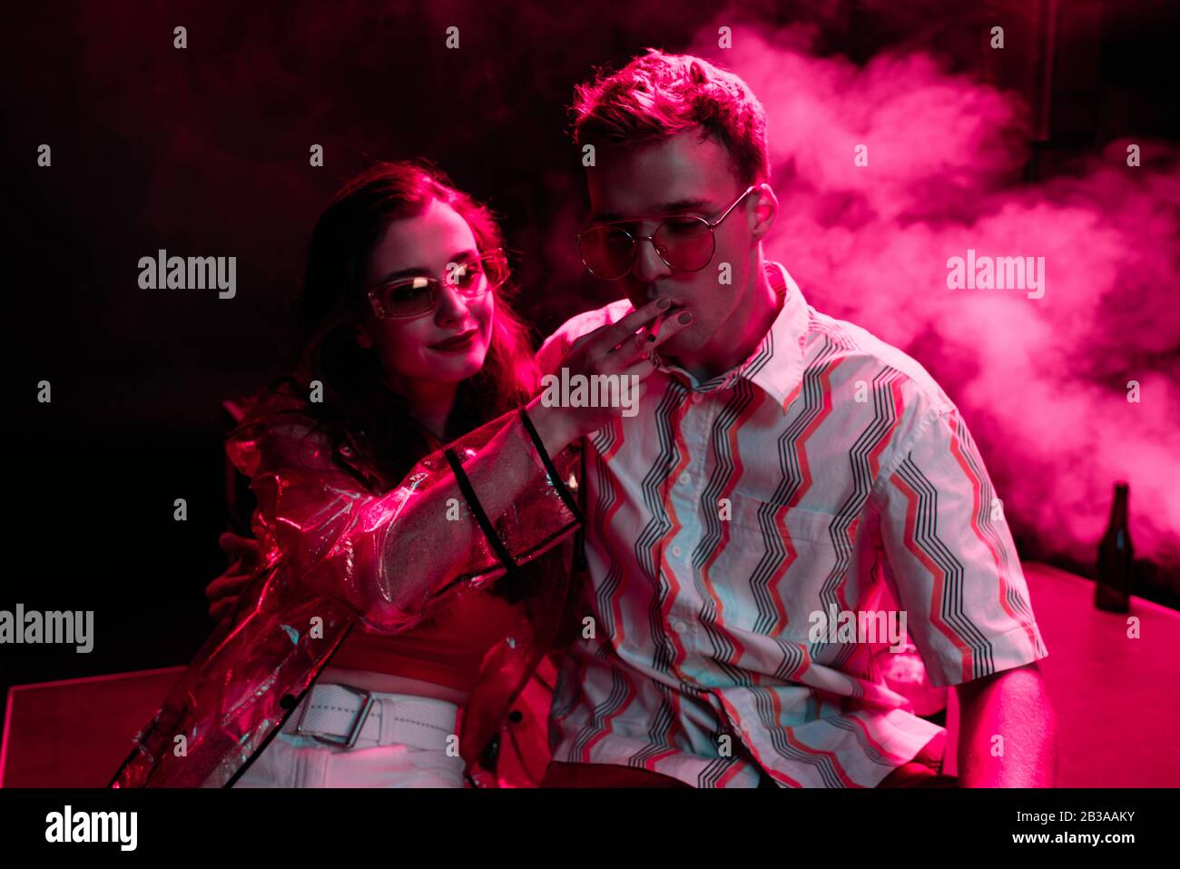 man smoking cigarette near young woman during rave party in nightclub ...