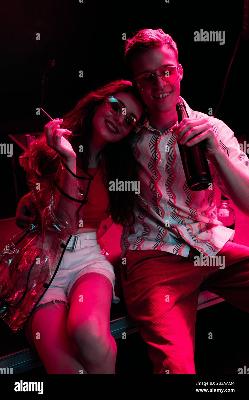 happy man with beer near girl with cigarette in nightclub during rave ...
