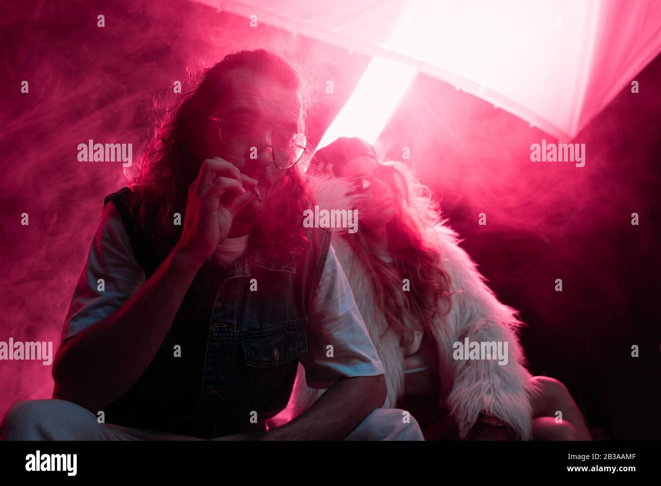 man smoking cigarette near young woman during rave party in nightclub ...