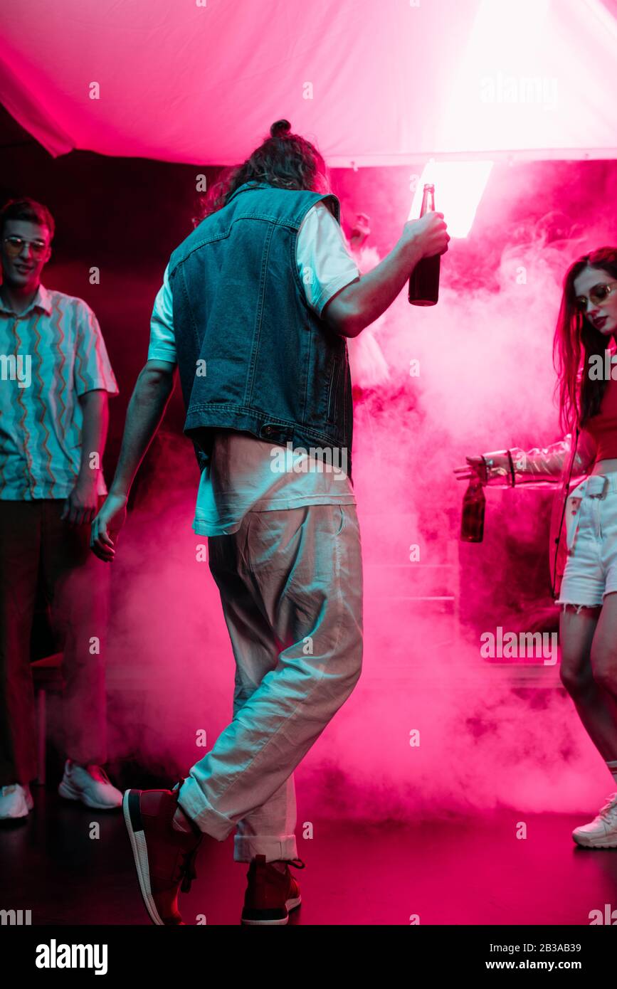 back view of man holding beer in nightclub and dancing during rave ...