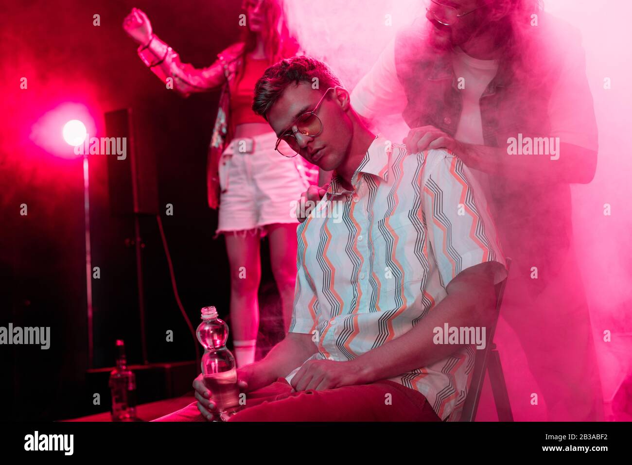 man checking on sick man sitting with bottle of water in nightclub ...