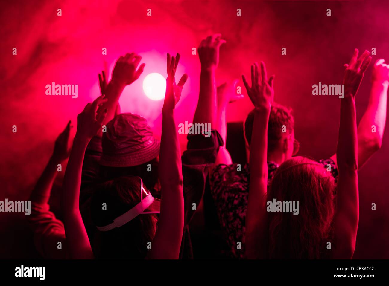 back view of people with raised hands during rave party in nightclub ...