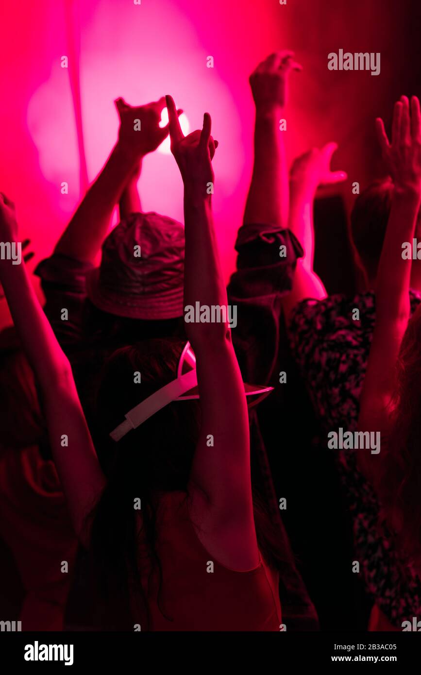 back view of people with raised hands during rave party in nightclub ...
