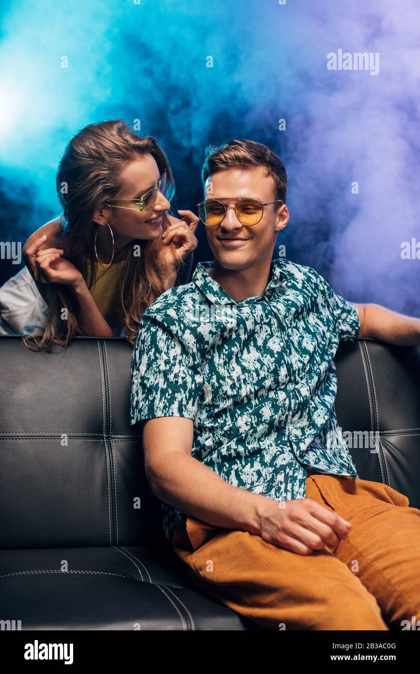 man siting on couch near young woman during rave party in nightclub ...
