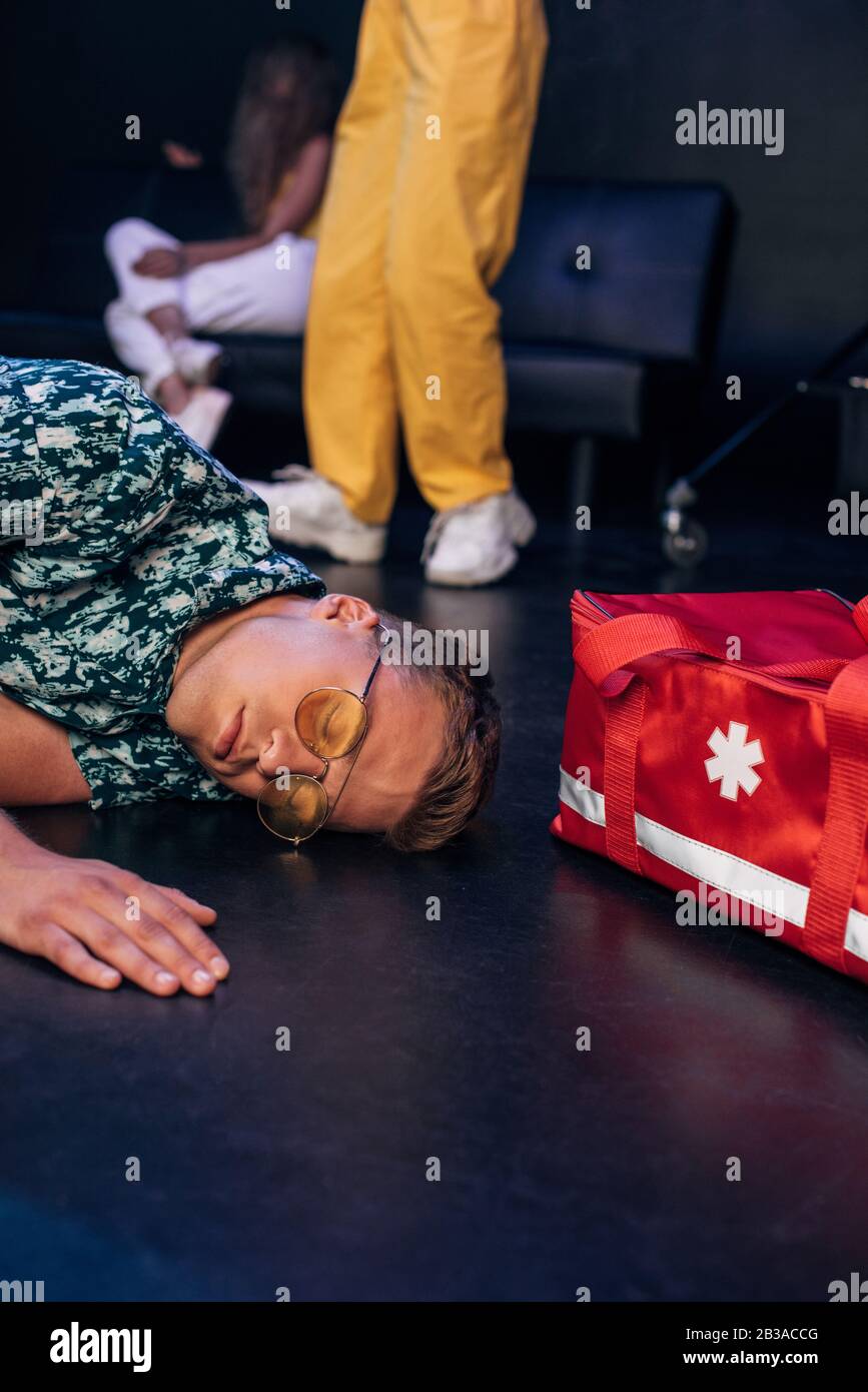 sick man in sunglasses lying on floor near first aid kit bag in ...