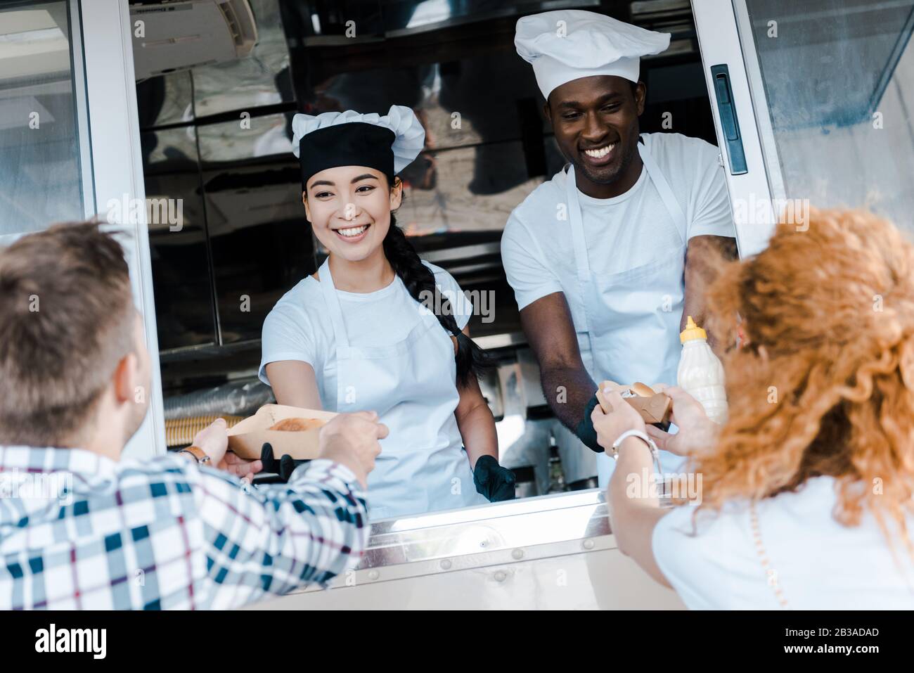 selective focus of happy multicultural chefs giving carton plates with ...
