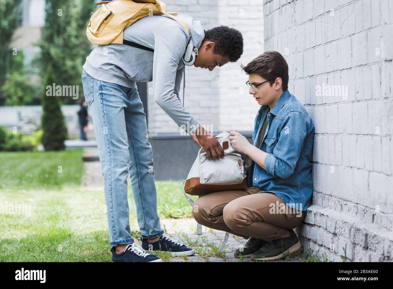 aggressive african american boy taking backpack from frightened boy in ...