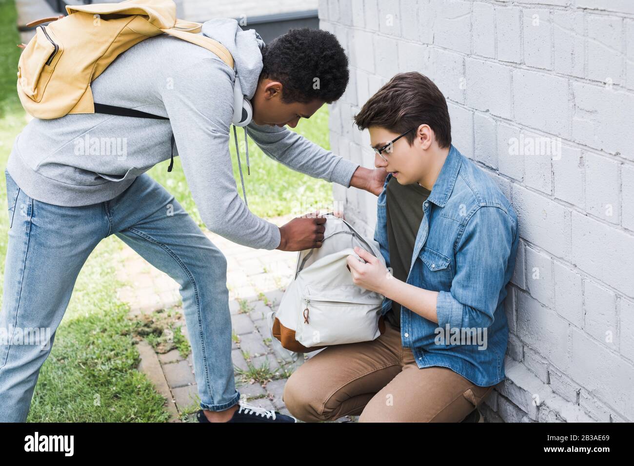 african american boy taking backpack from frightened boy in glasses ...