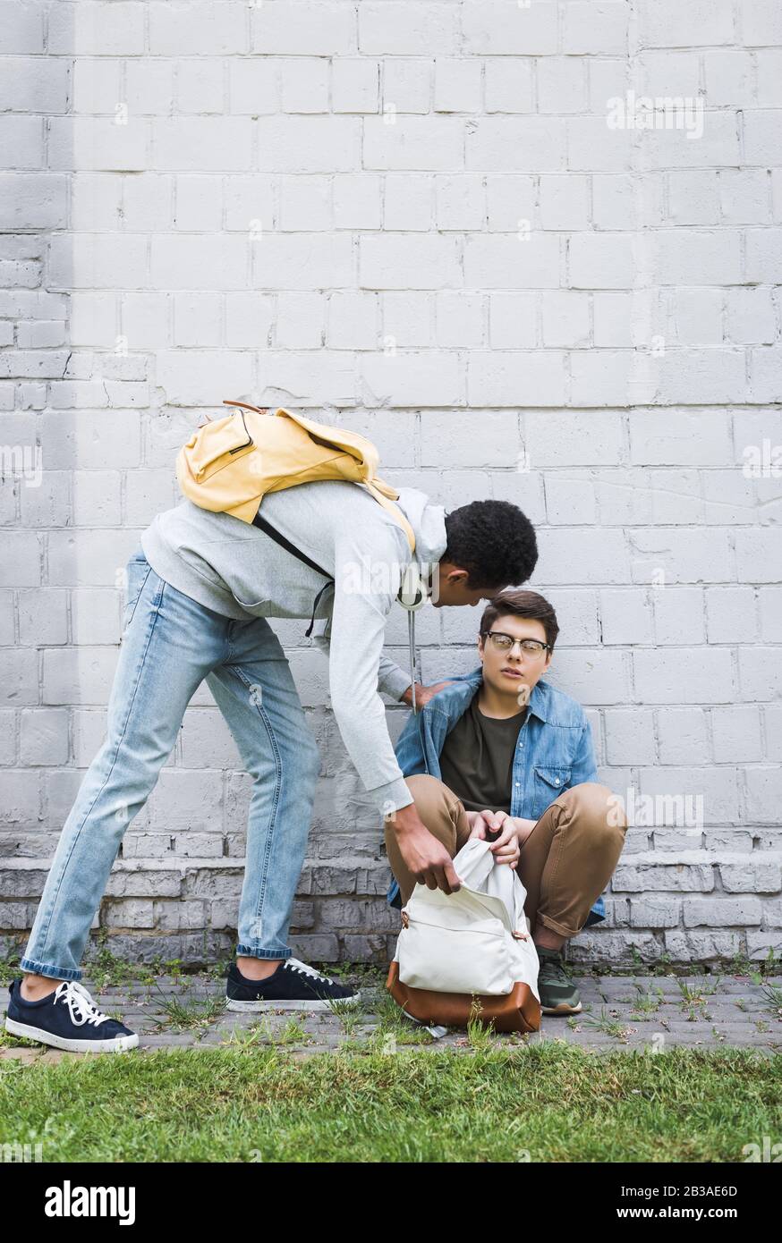 aggressive african american boy taking backpack from frightened boy in ...