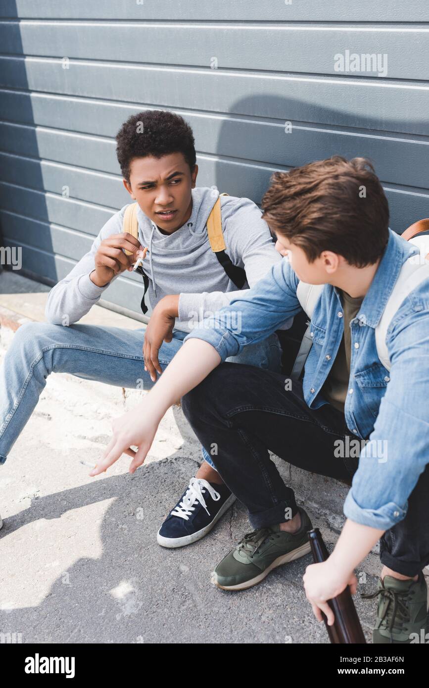 friends sitting, talking, holding beer and smoking cigarettes outside ...