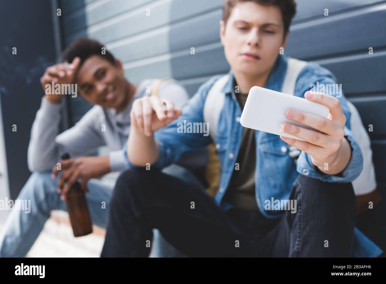 selective focus of friends smiling, smoking cigarettes, holding beer ...