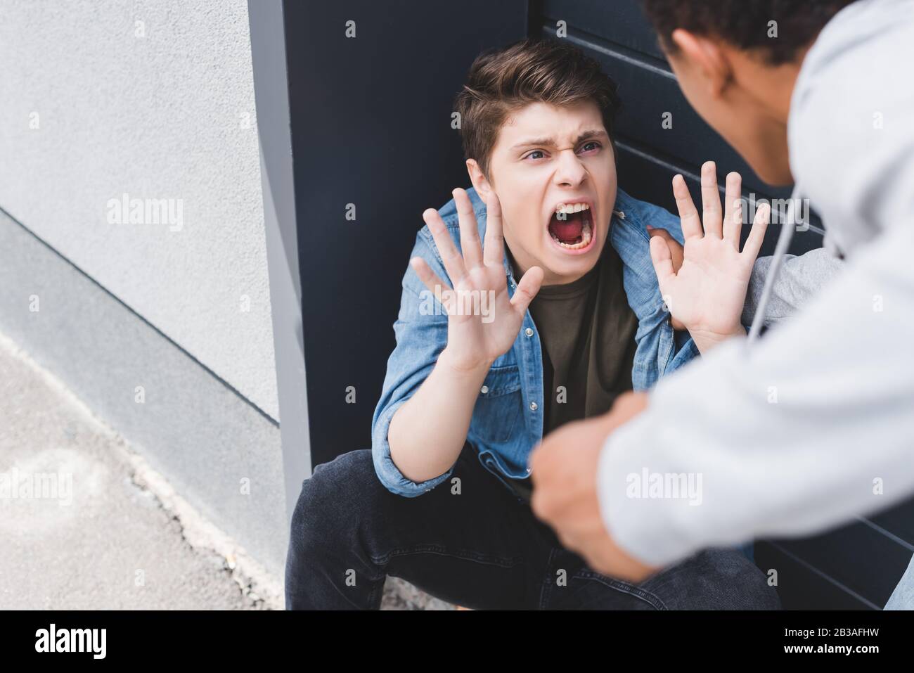 selective focus of african american boy punching scared and yelling boy ...