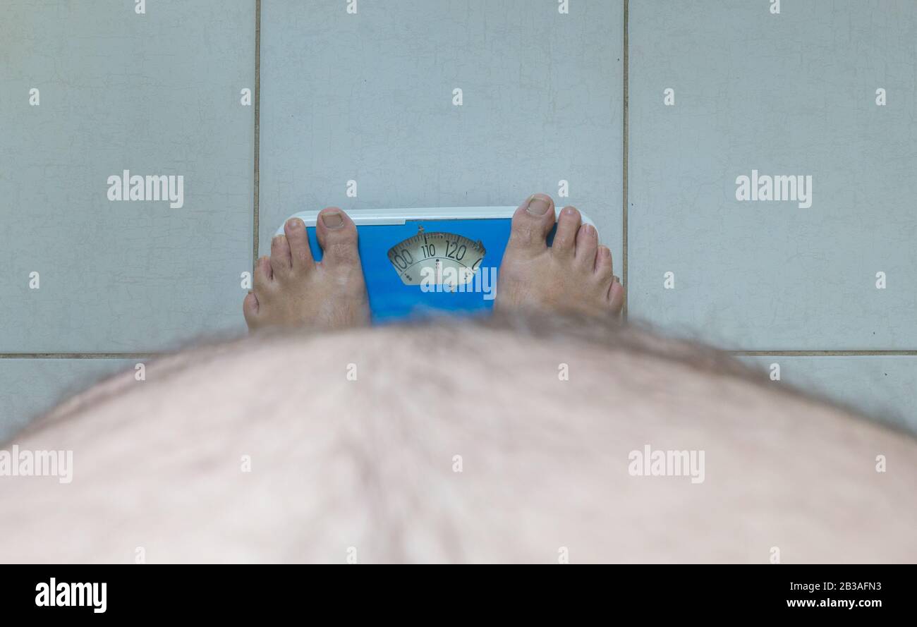 Overweight man standing on floor scales indoors Stock Photo - Alamy