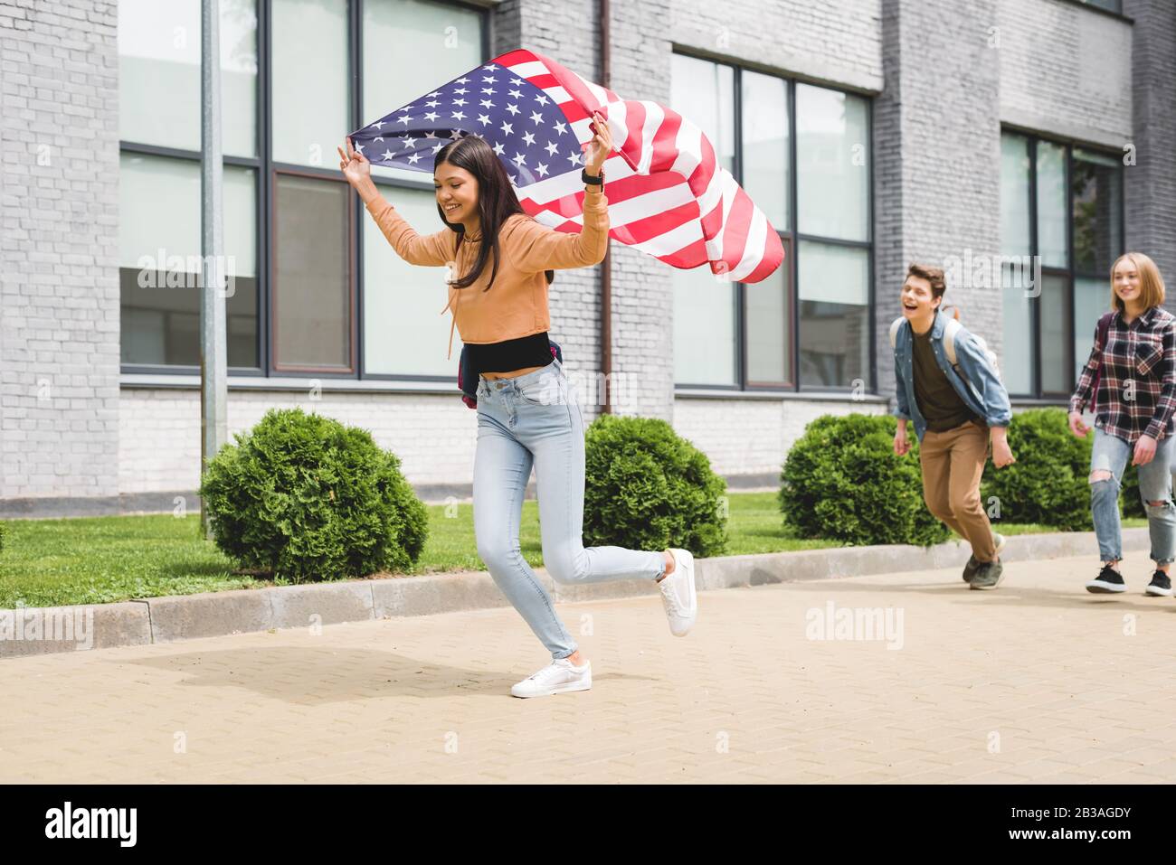happy teenagers smiling, holding american flag and running outside ...