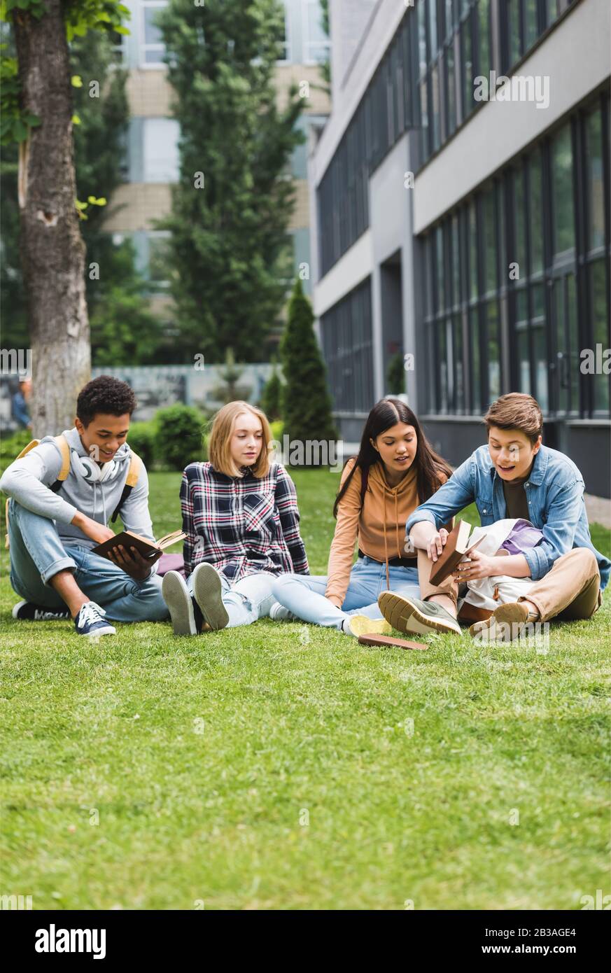 smiling teenagers sitting on grass and reading books outside Stock ...