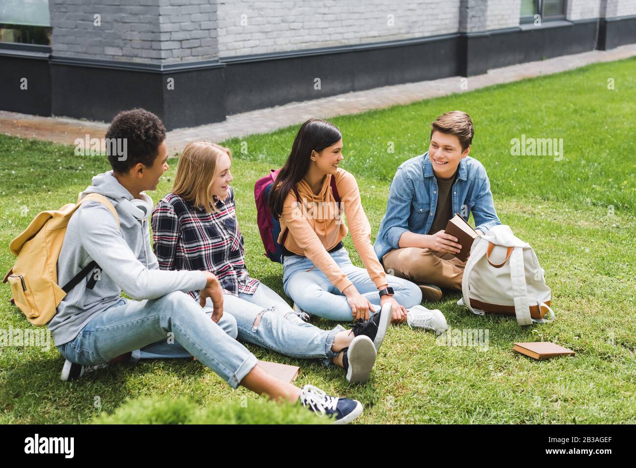 smiling teenagers sitting on grass, talking, holding book outside Stock ...