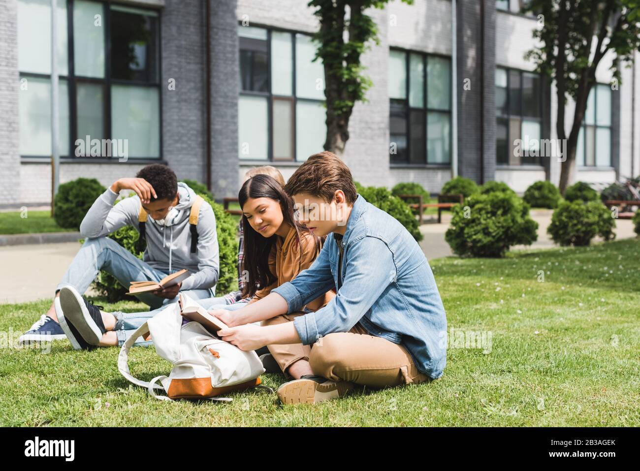 teenagers sitting on green grass and reading books outside Stock Photo ...