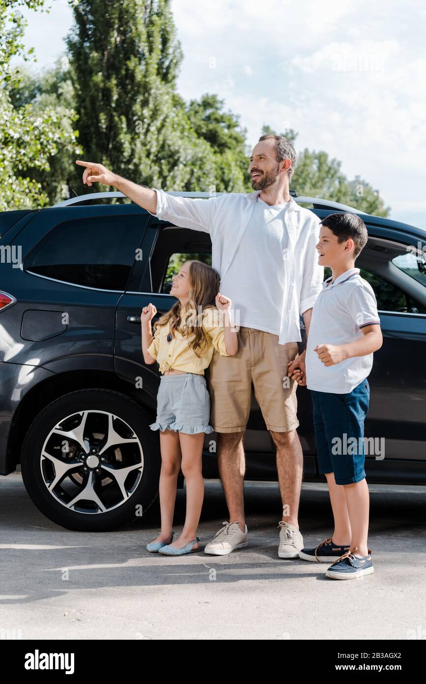 happy father pointing with finger while standing with cheerful kids and ...