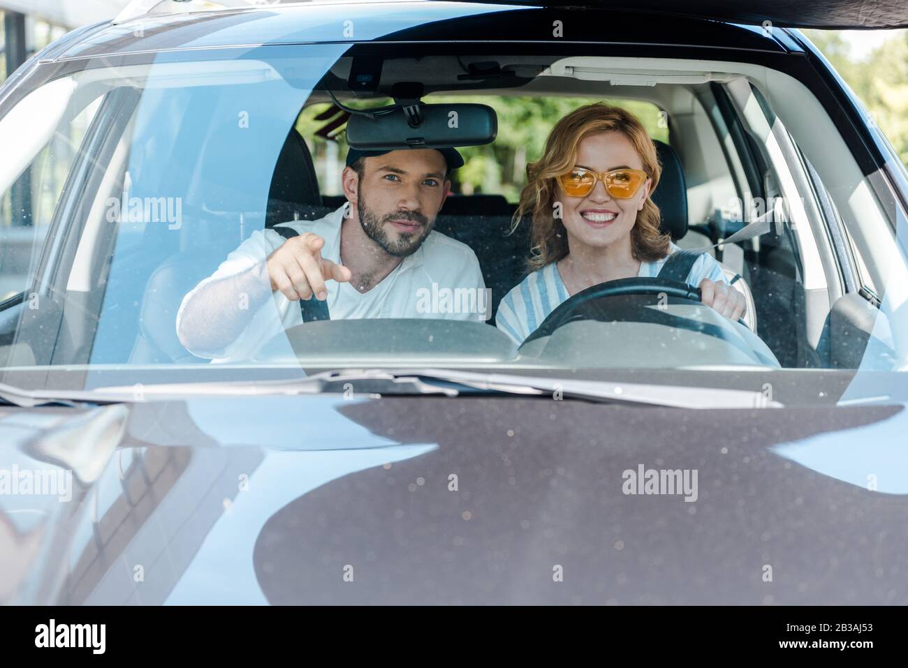 selective focus of man pointing with finger while woman driving car ...