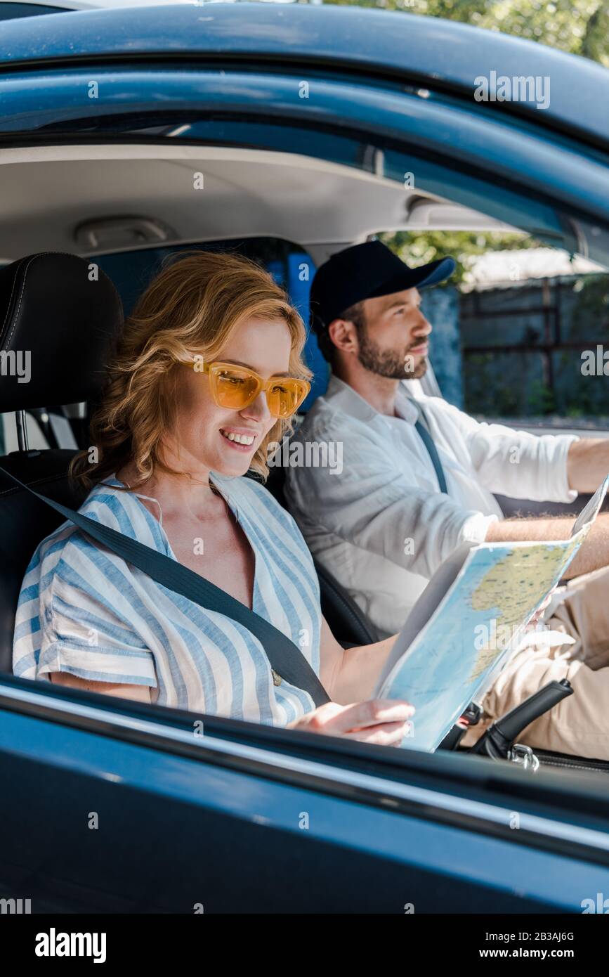 selective focus of cheerful woman holding map while man driving car ...