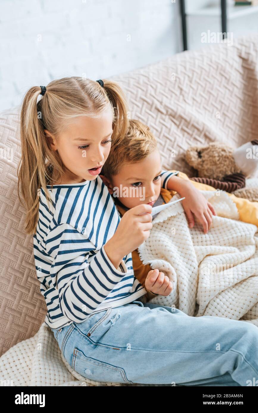 shocked sister looking at thermometer while hugging sick brother Stock ...