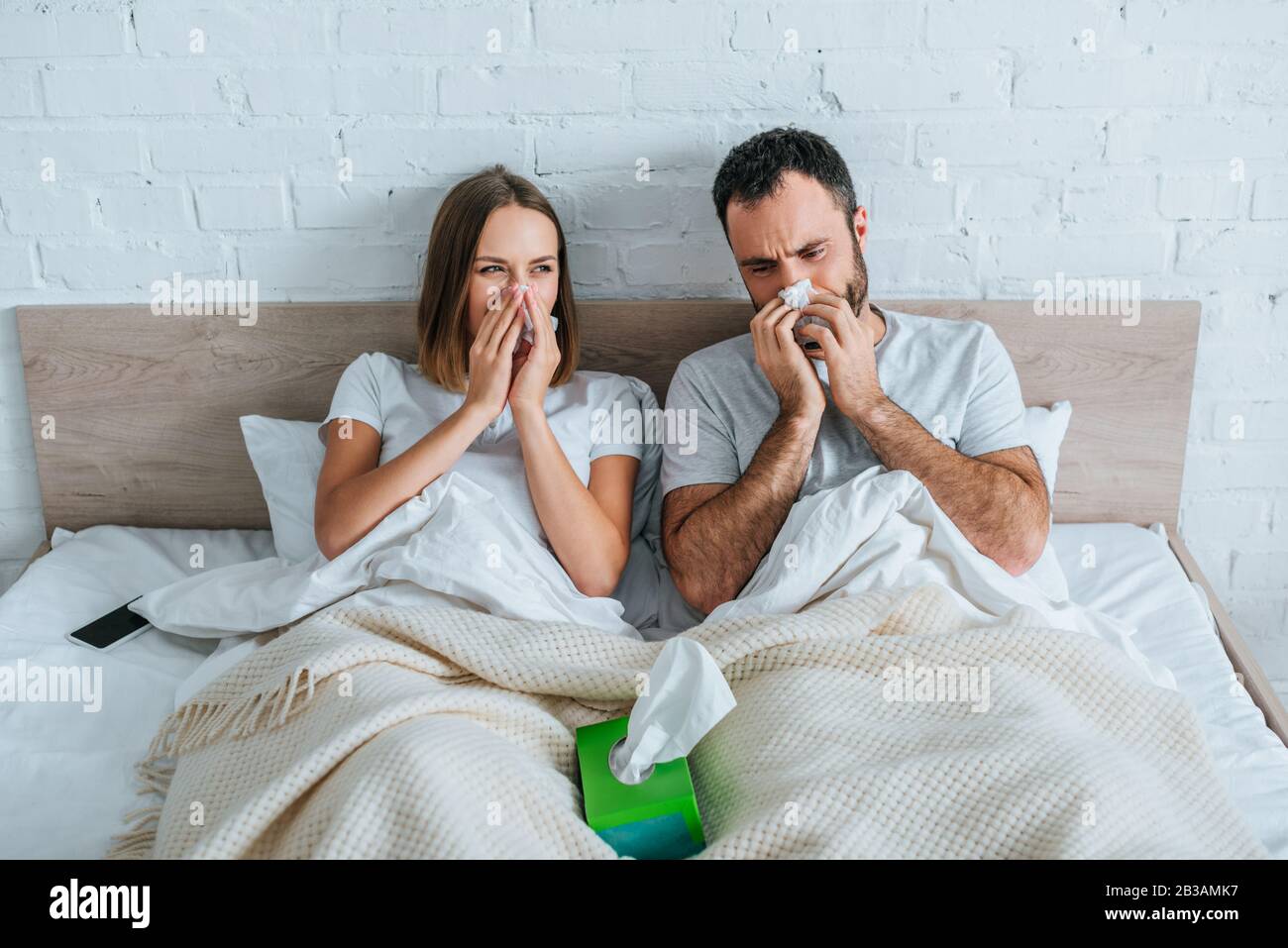 diseased husband and wife sneezing while lying in bed together Stock ...