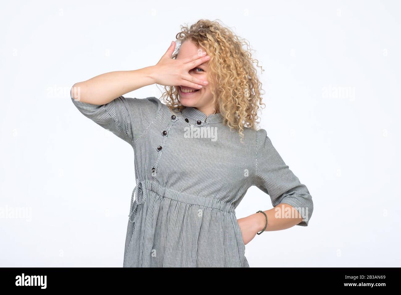 Shy timid teenage curly girl covering face with hands and peeping ...