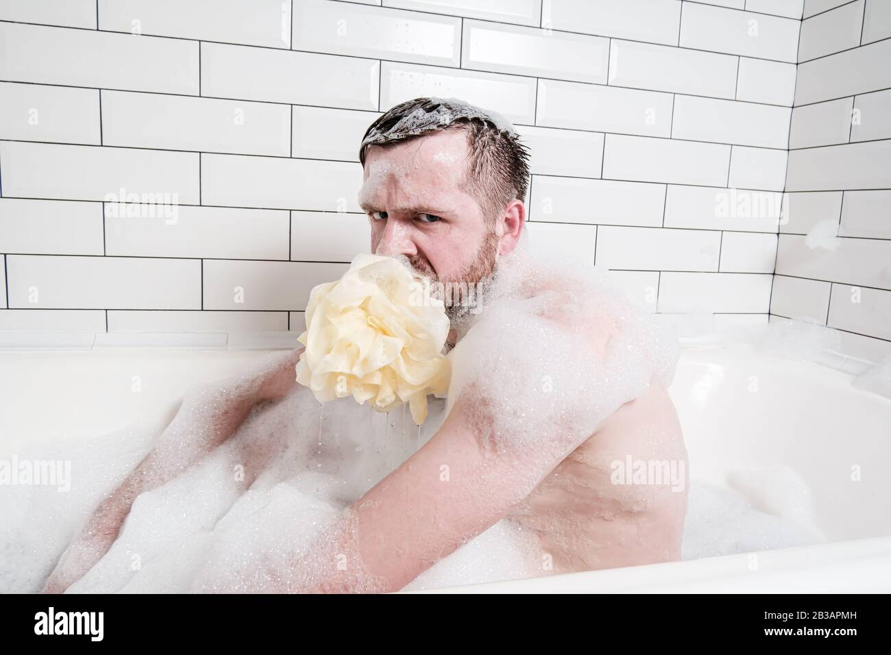 Displeased, weird man with a soapy sponge puff in mouth, sits in a ...
