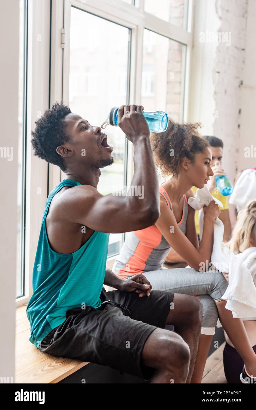 Side view of multicultural dancers drinking water while resting in ...
