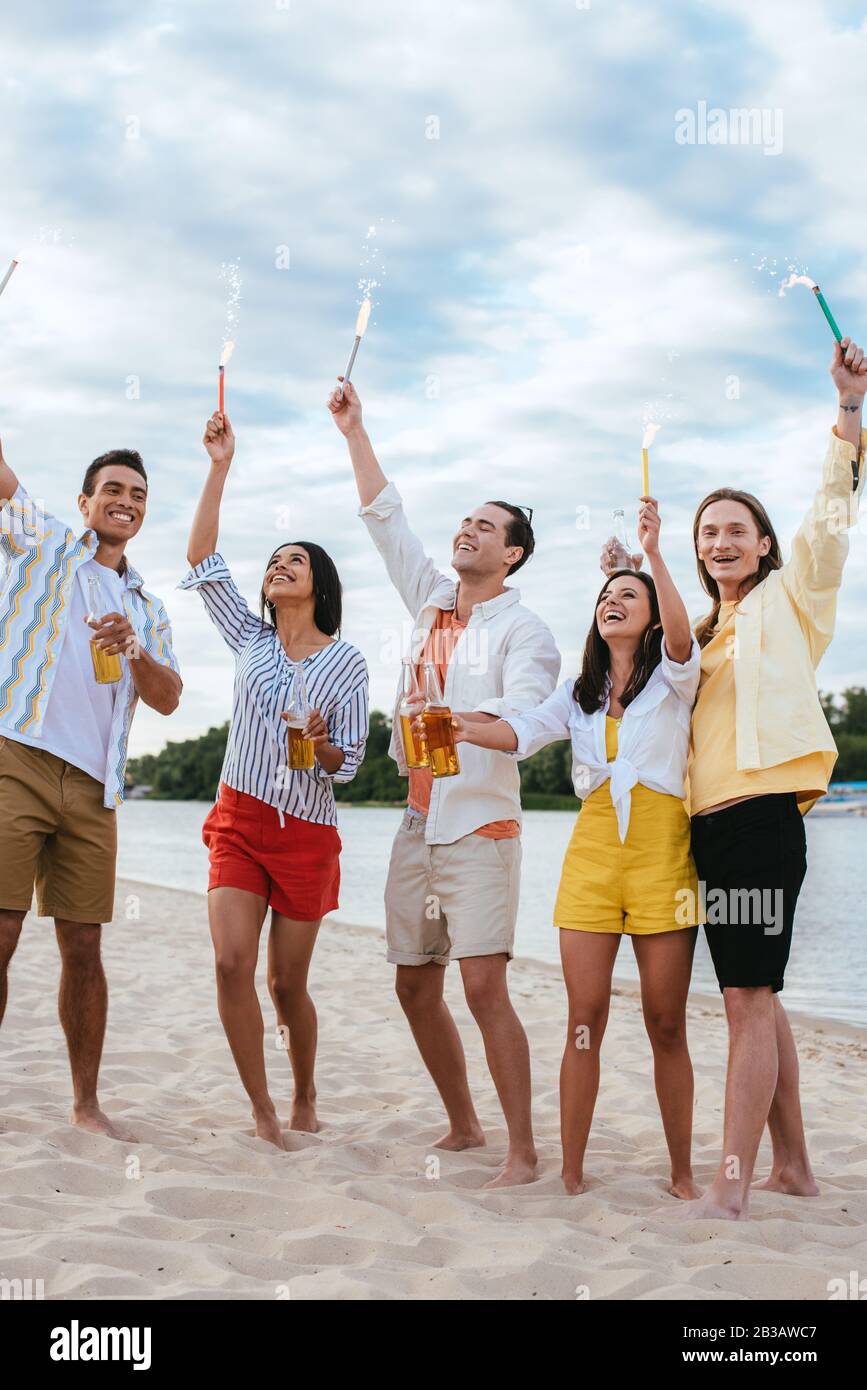 cheerful multicultural friends having fun on beach while holding ...