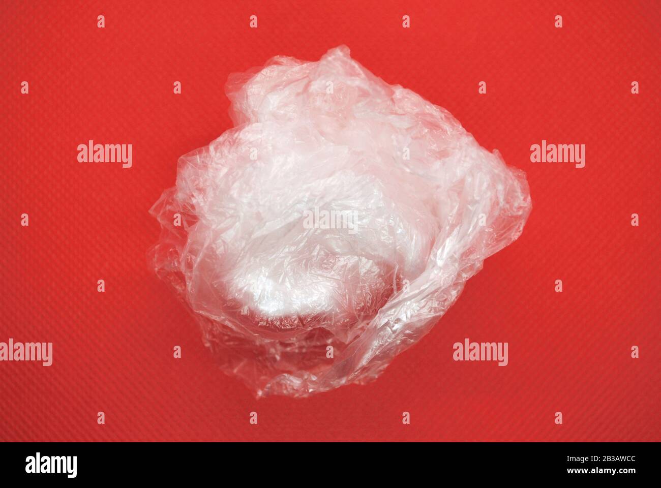 Crushed white clear transparent polyethylene plastic bag on a red ...