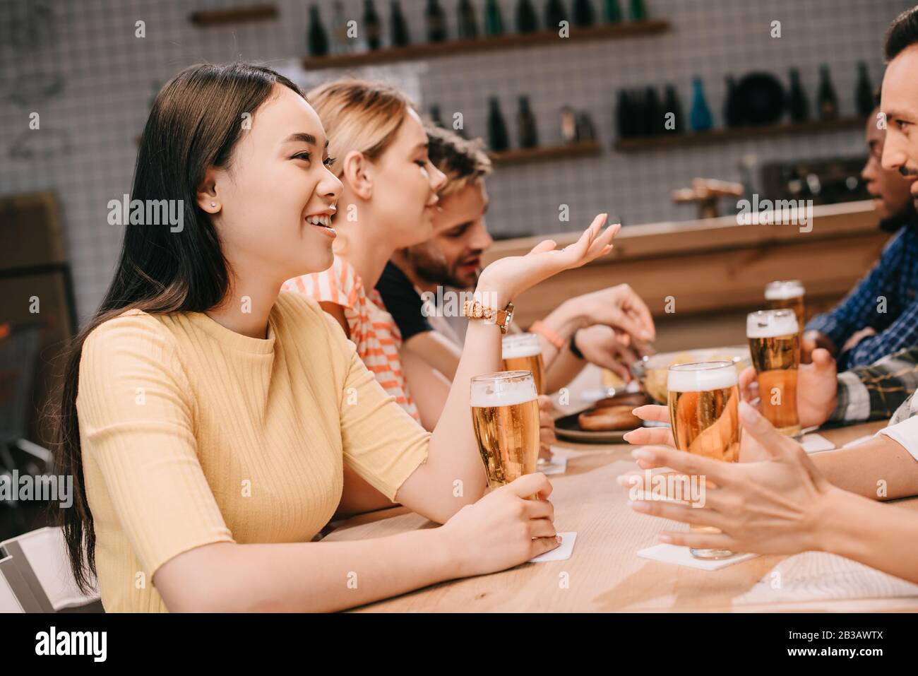 happy multicultural friends talking while drinking beer together in pub ...