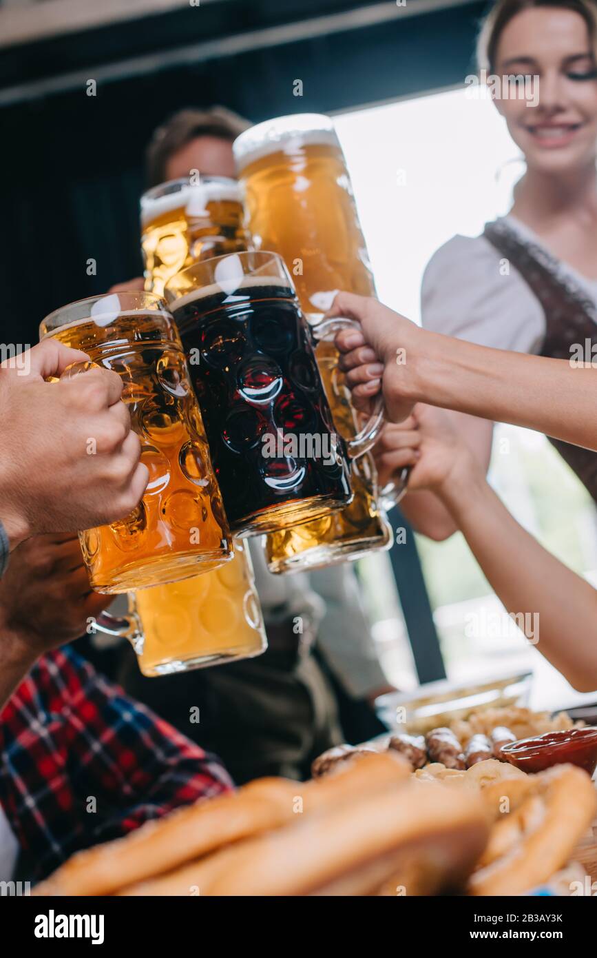 partial view of friends clinking mugs of light and dark beer while ...