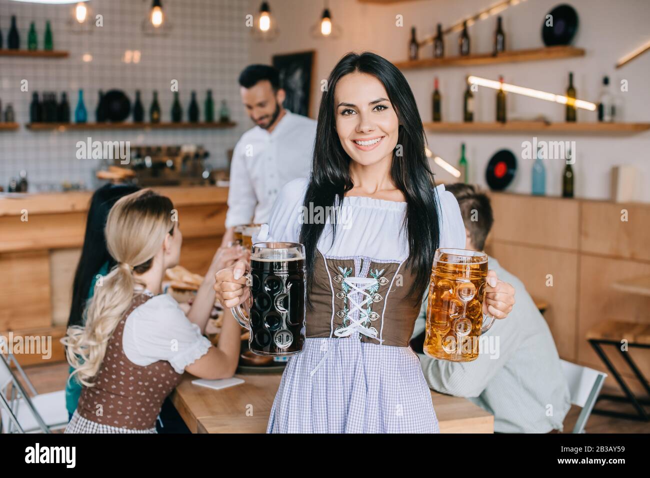 beautiful waitress in traditional german costume holding mugs of light ...