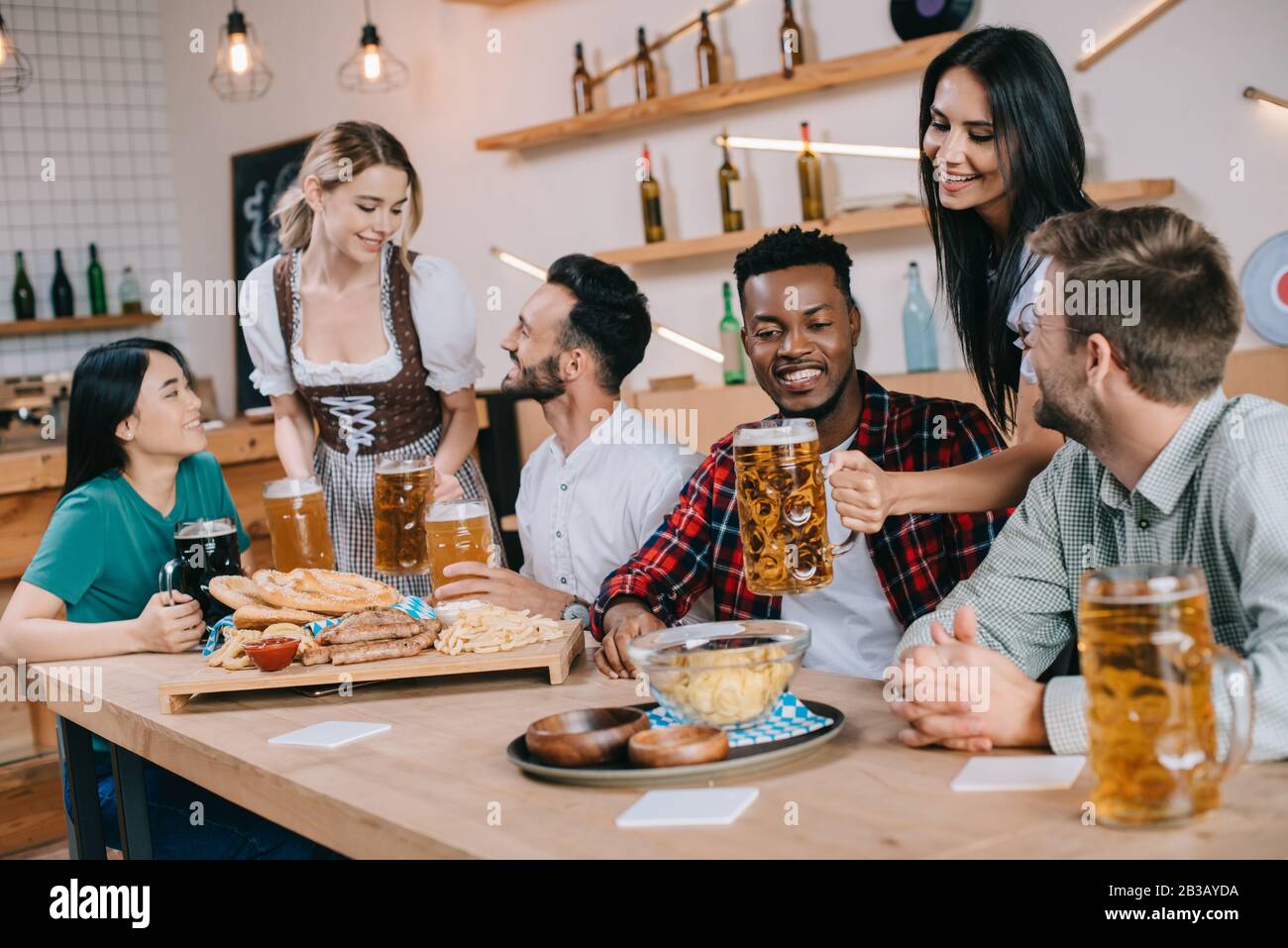two attractive waitresses serving beer for multicultural friends in pub ...
