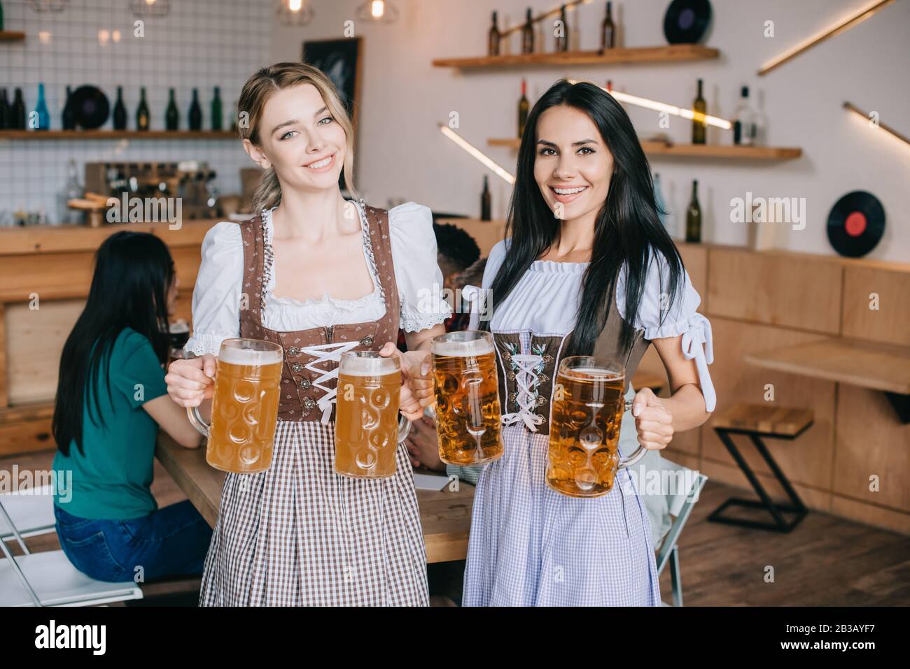two beautiful waitresses in traditional german costumes holding mugs ...