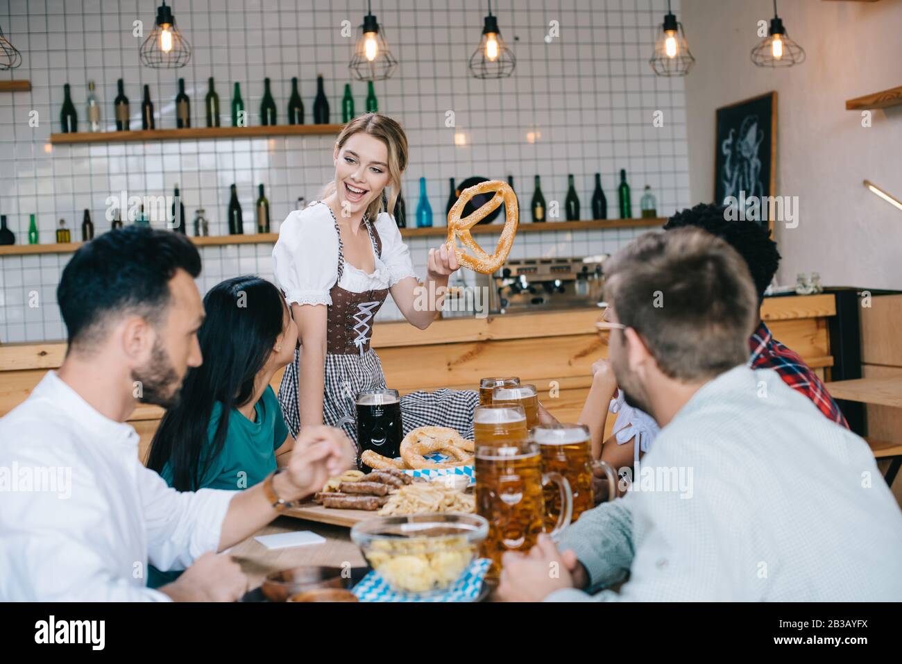 cheerful waitress in traditional german costume holding pretzel while ...
