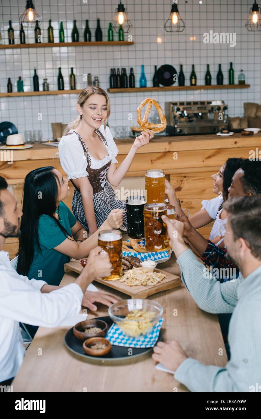 cheerful waitress in traditional german costume holding pretzel while ...